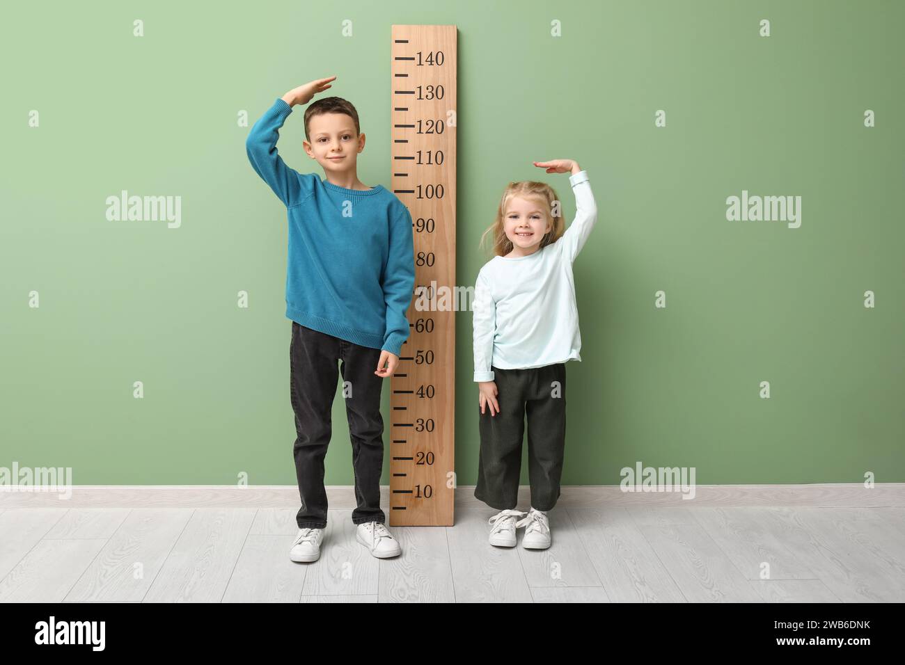 Cute little children measuring height near green wall Stock Photo - Alamy