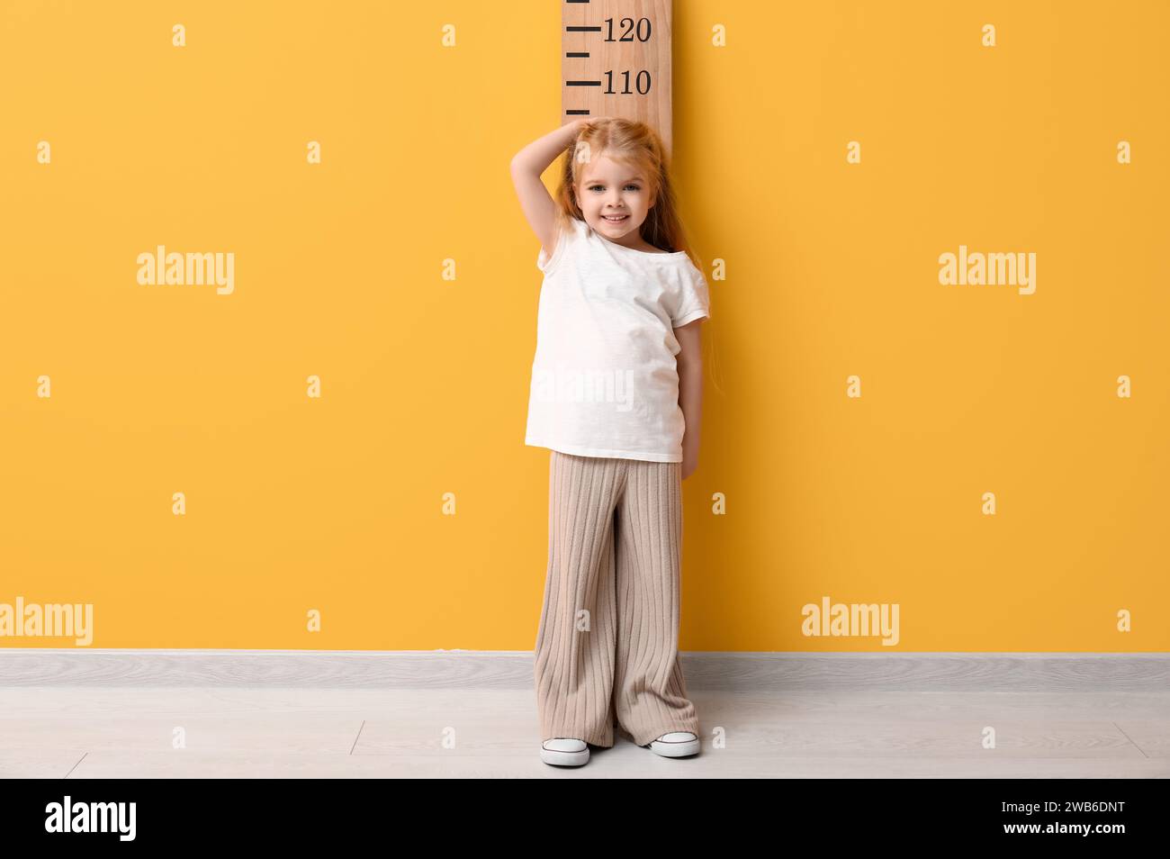Cute little girl measuring height near yellow wall Stock Photo - Alamy
