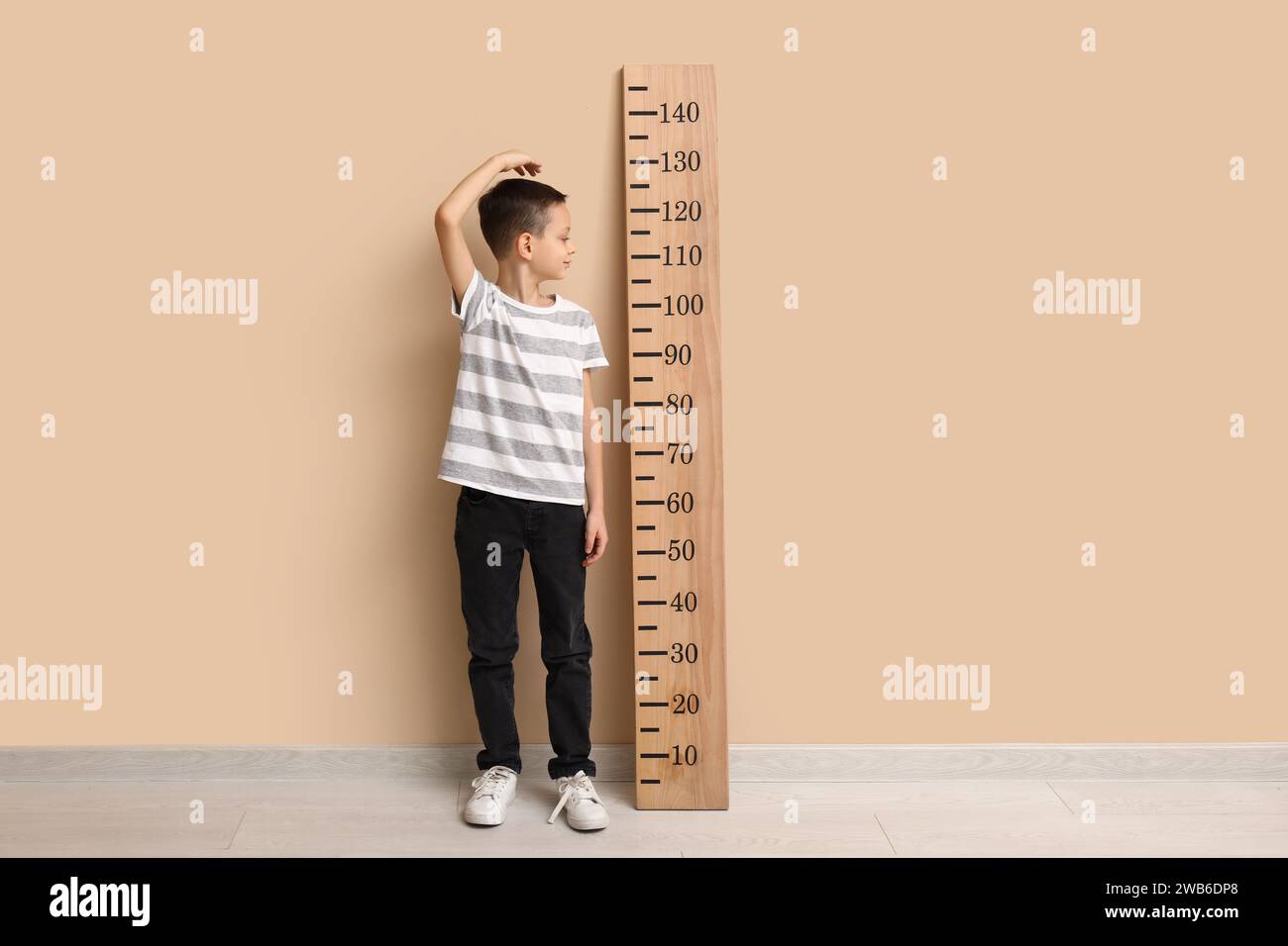 Cute little boy measuring height near beige wall Stock Photo - Alamy