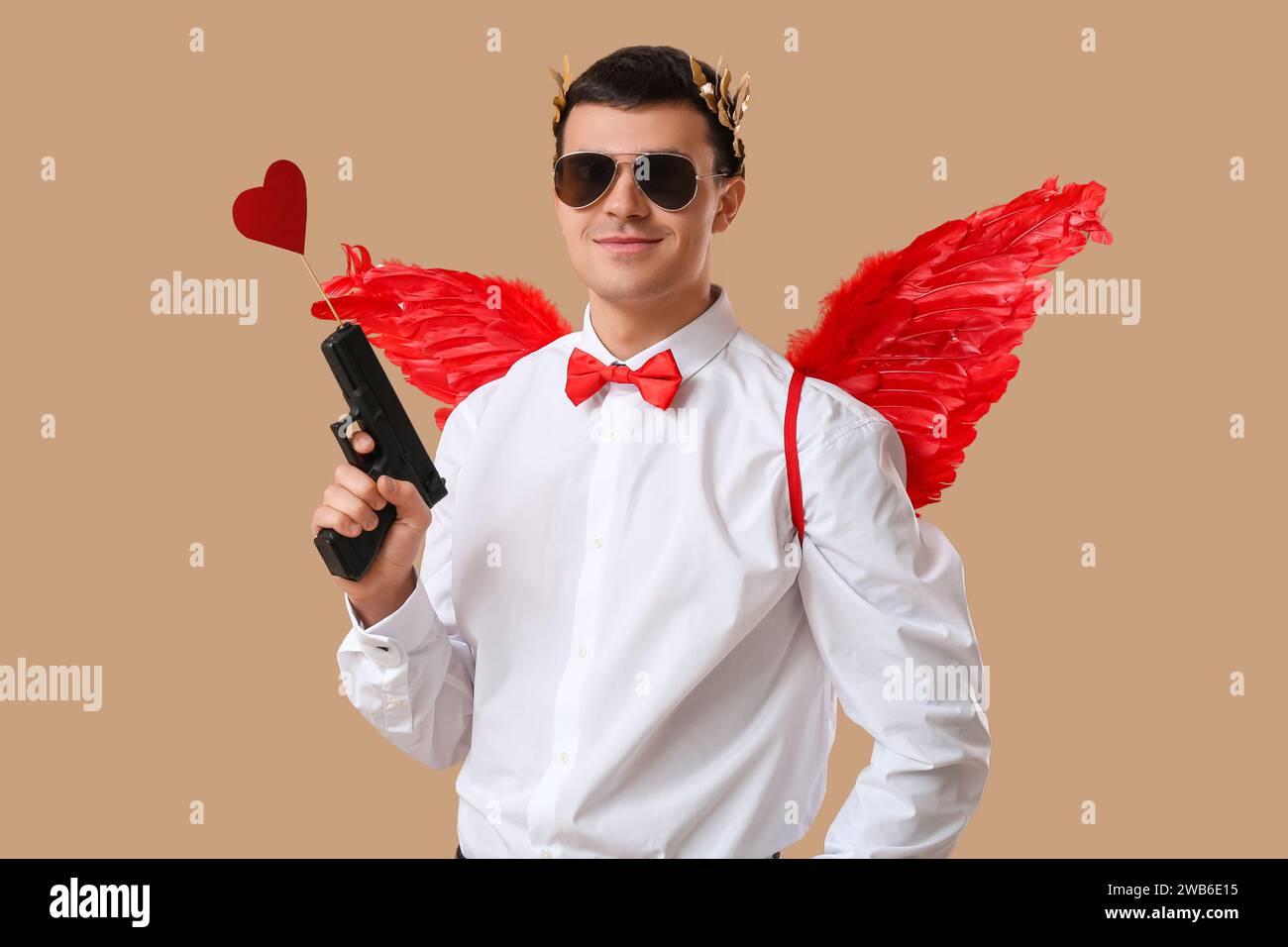 Cool young man dressed as Cupid with gun on beige background. Valentine ...