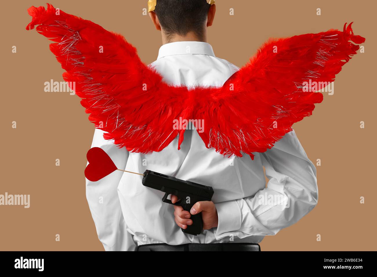 Cool young man dressed as Cupid with gun on beige background, back view ...