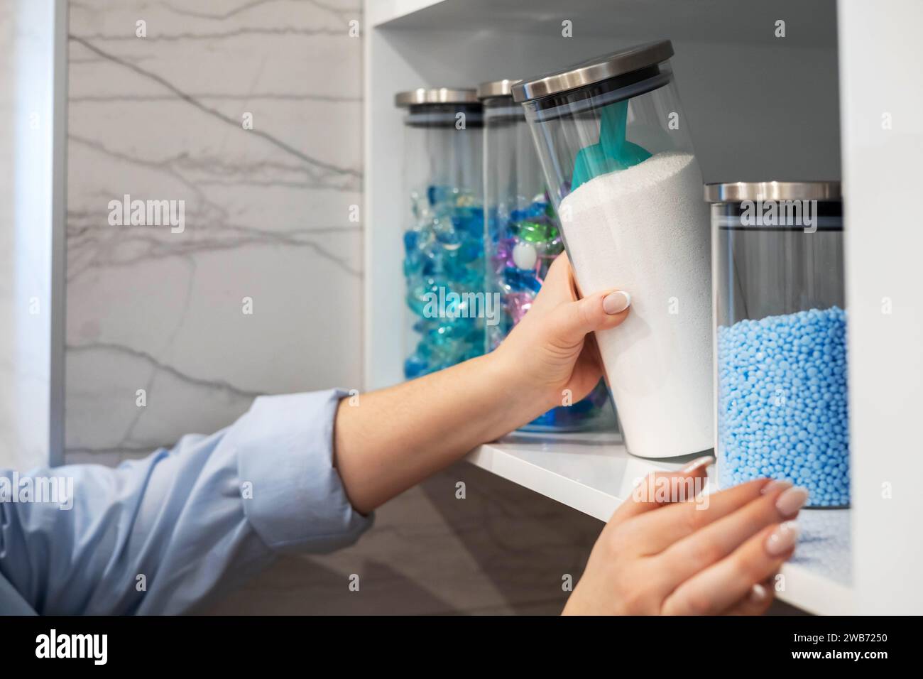 Woman housewife hands putting glass can washing powder laundry capsule ...
