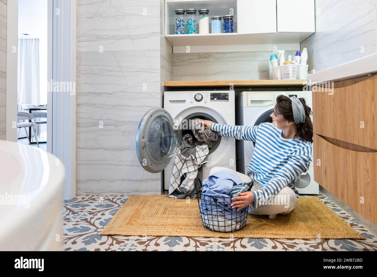 Modern housewife putting dirty linen textile and clothes to washing ...