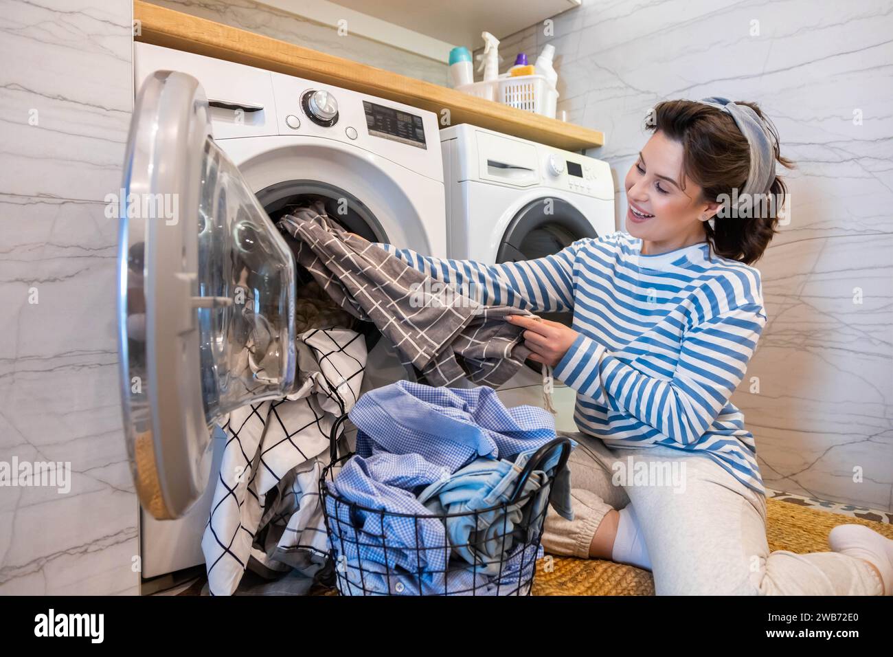 Modern housewife putting dirty linen textile and clothes to washing ...