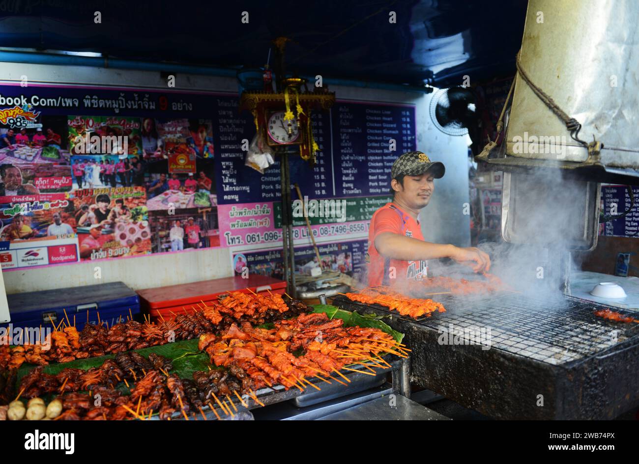 A Thai man grilling chicken at a small street food on Soi Naradhiwas ...
