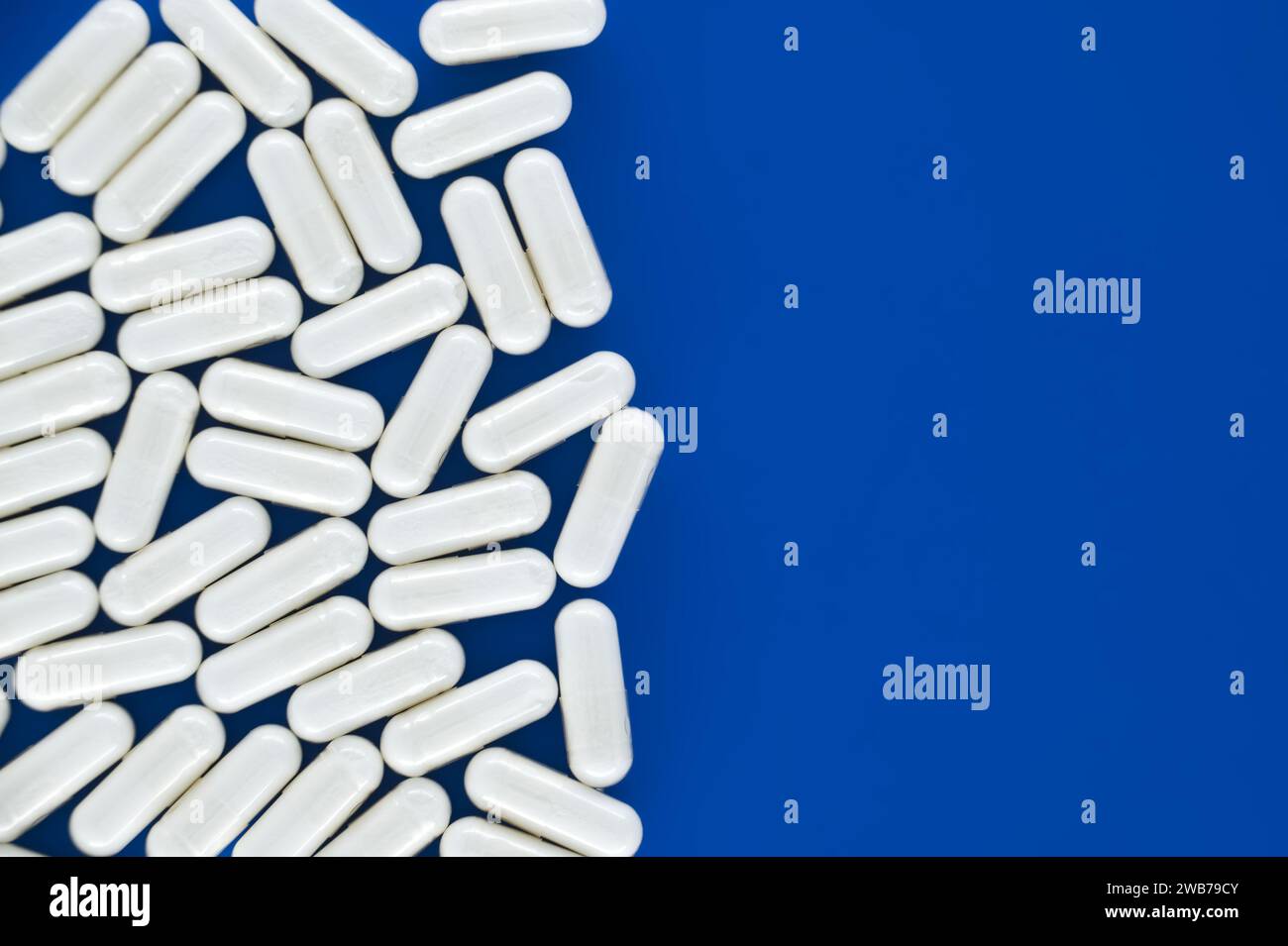 Large number of white pills scattered on a blue surface. Minimal ...