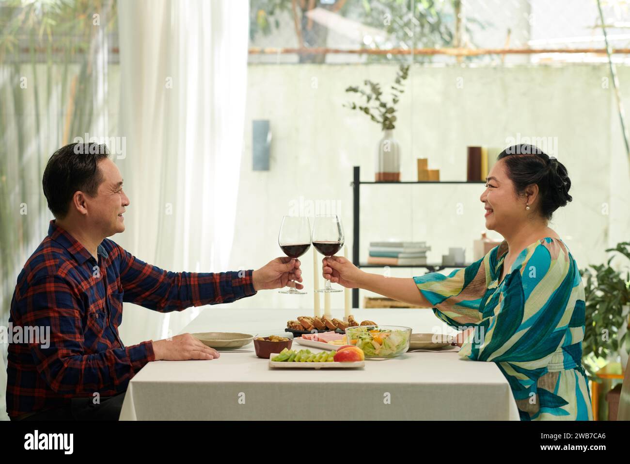 Elderly couple toasting with glasses of wine over dinner table Stock ...