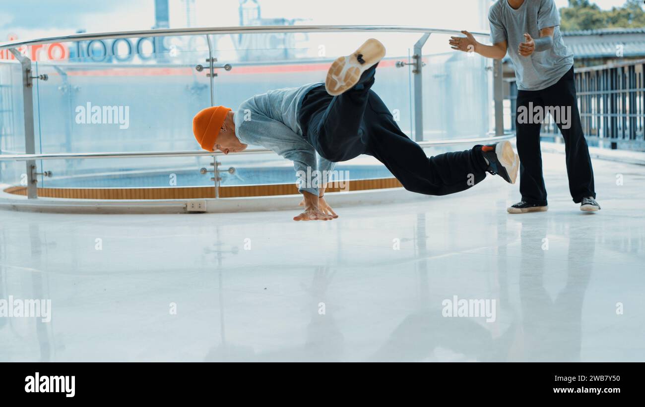 Hipster perform break dance while friend encourage him at mall. Diverse ...