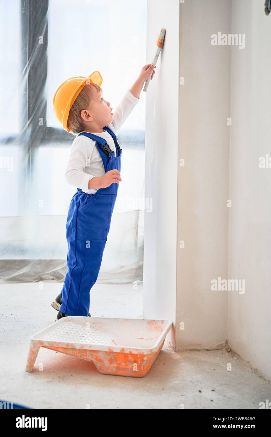 Full length of child construction worker painting wall with paint brush ...
