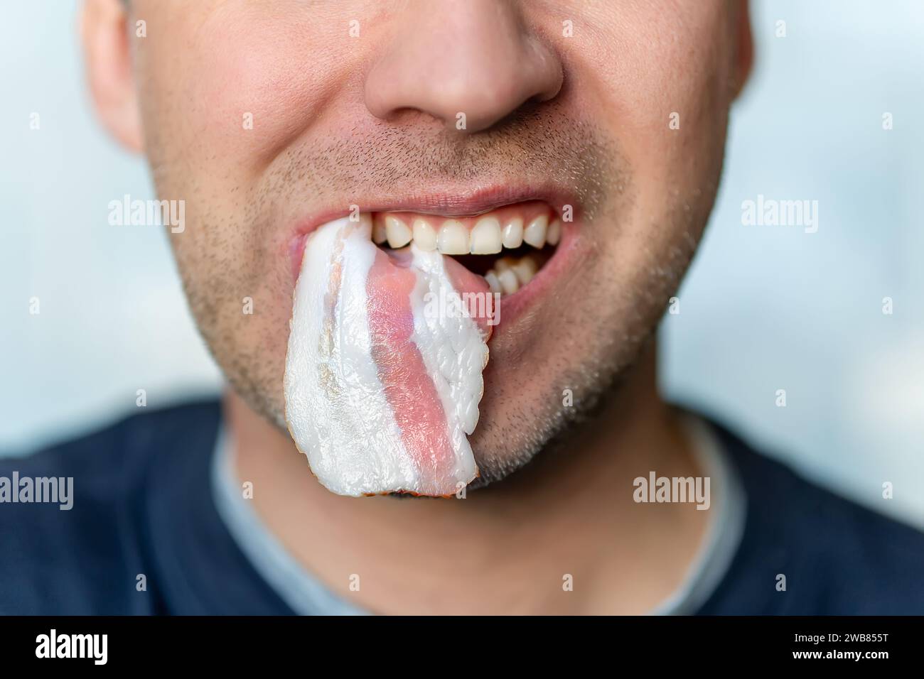 fat bacon in a male mouth in close-up. A man eats unhealthy fatty food ...