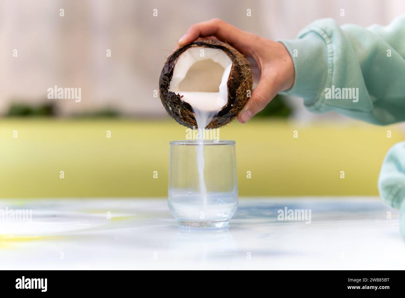 Female hand pouring coconut milk from coconut into a bowl and glass ...