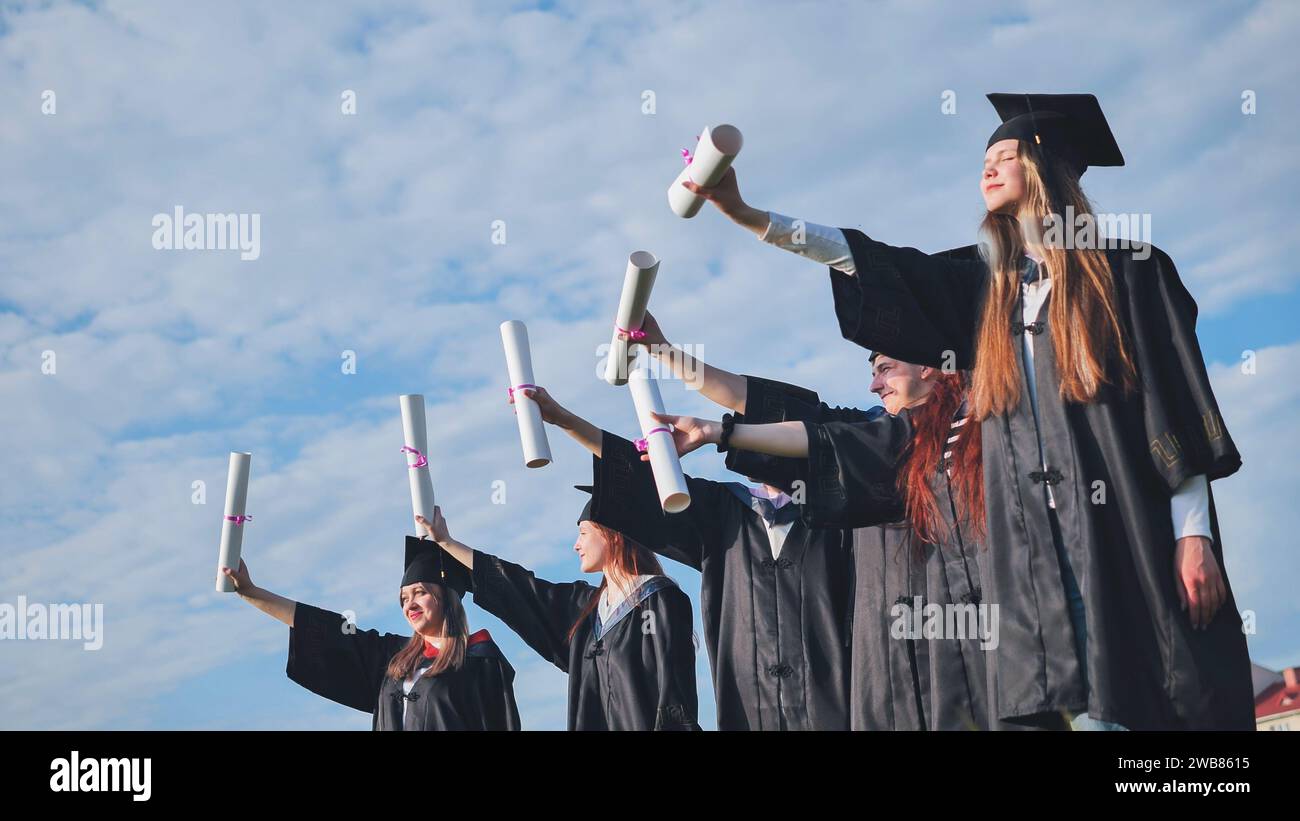 Cheerful graduates pose with raised diplomas on a sunny day Stock Photo ...