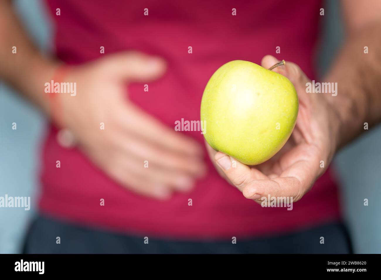 Young man holding apple wearing red shirt cover blue background with ...