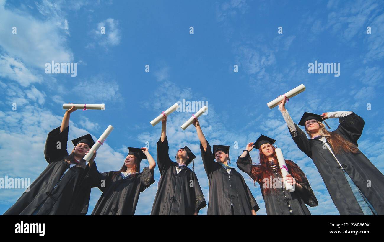 Cheerful graduates pose with raised diplomas on a sunny day Stock Photo ...
