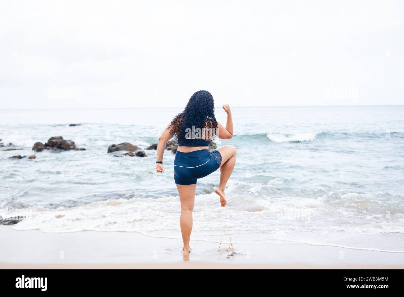 Fitness woman, standing, doing leg exercises on the beach sand with her ...