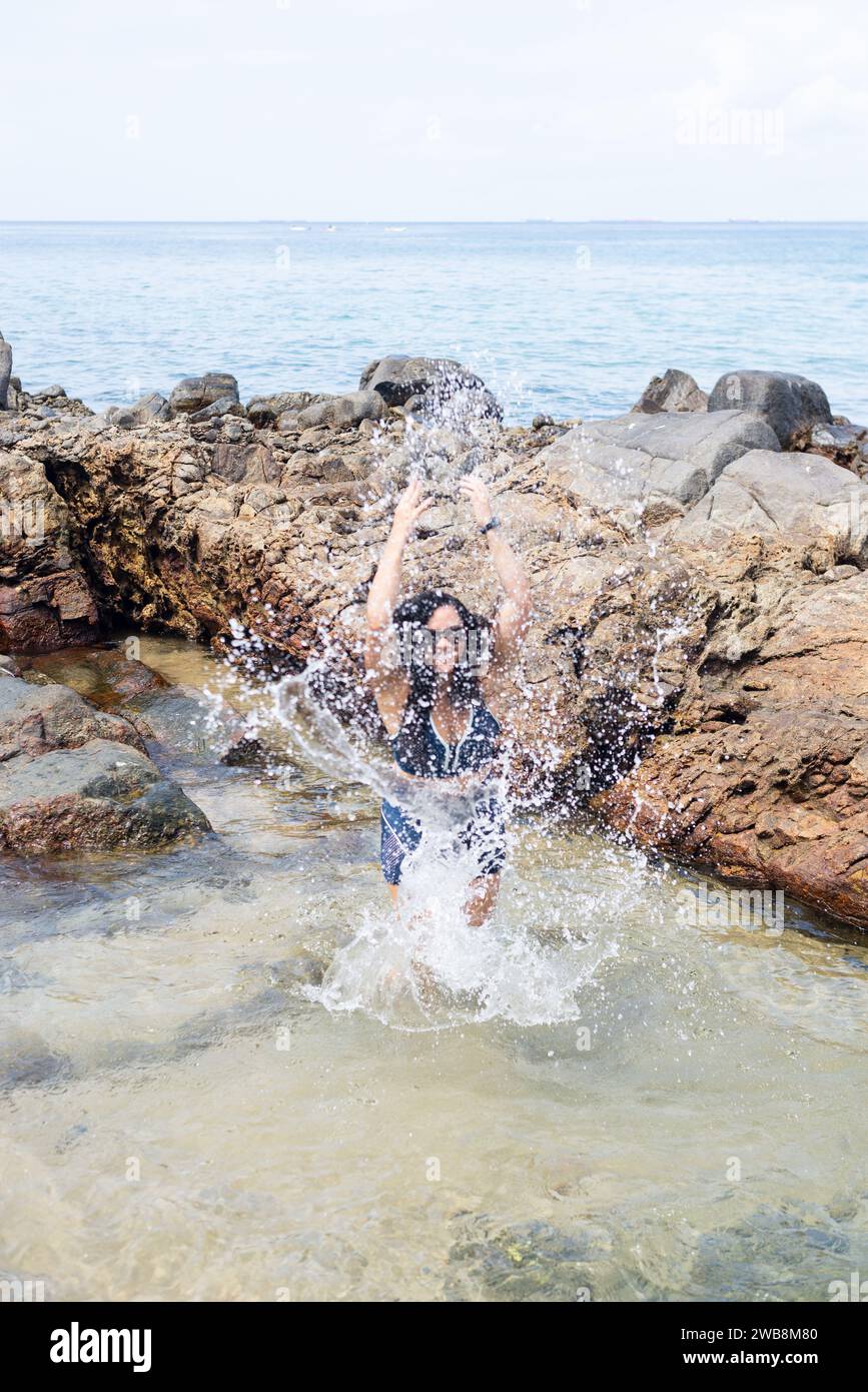 Beautiful woman in a puddle on the beach, throwing water into the air ...