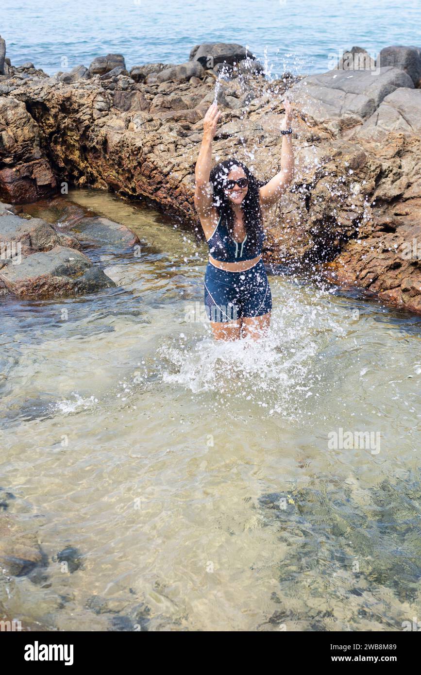 Beautiful woman in a puddle on the beach, throwing water into the air ...