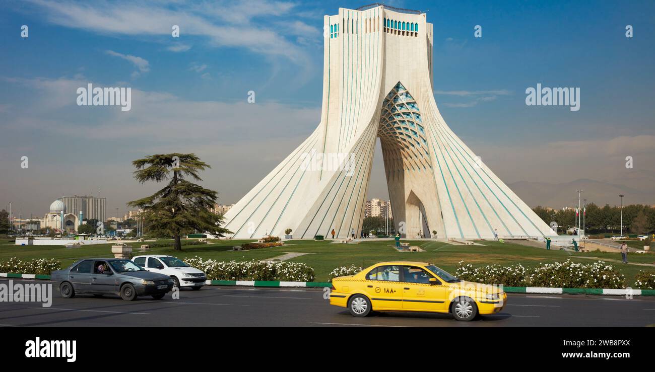 Yellow taxi passes by the Azadi Tower (Freedom Tower), an iconic ...