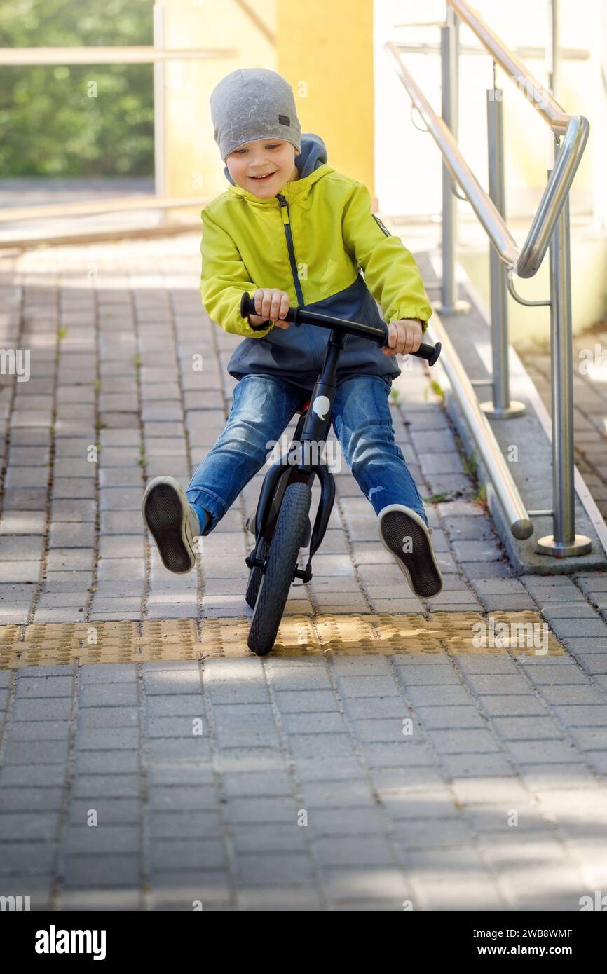 A little boy rides his balance bike downhill, he lifts both legs and ...