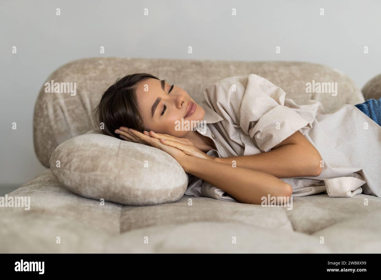 Tired young woman lying on cozy couch take nap daydreaming in living room, peaceful girl relax ...