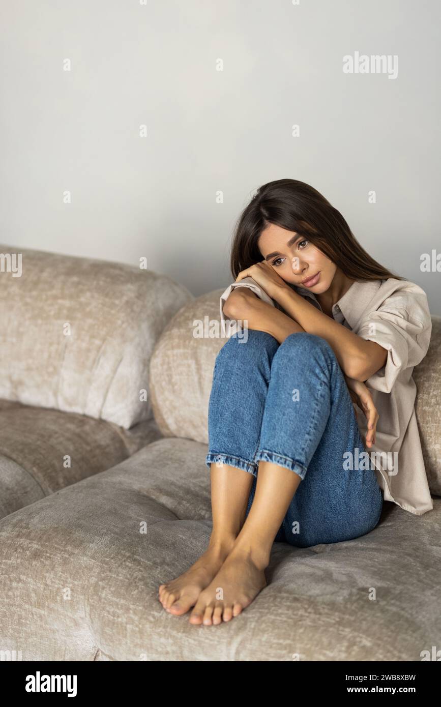 Sad depressed woman at home sitting on the couch, looking down and ...