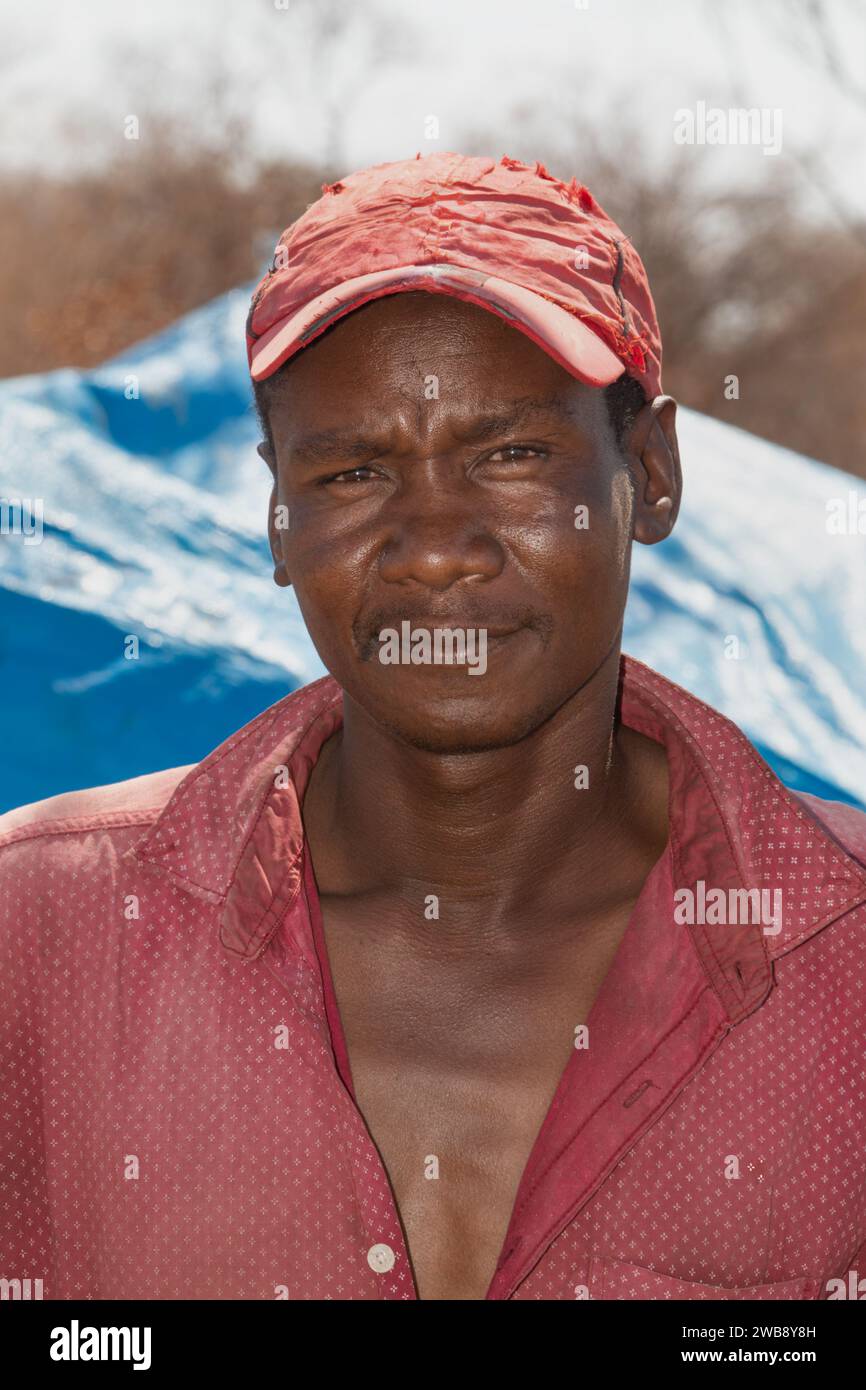 portrait of an african man standing in front of a shack in a refugee ...