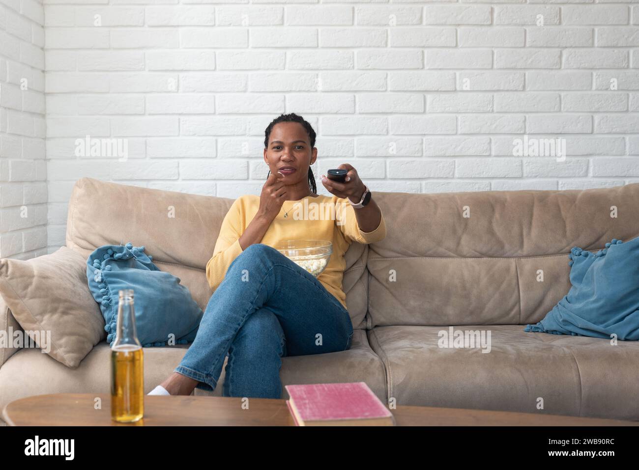 Laughing young pretty African American woman sitting on sofa, eating ...