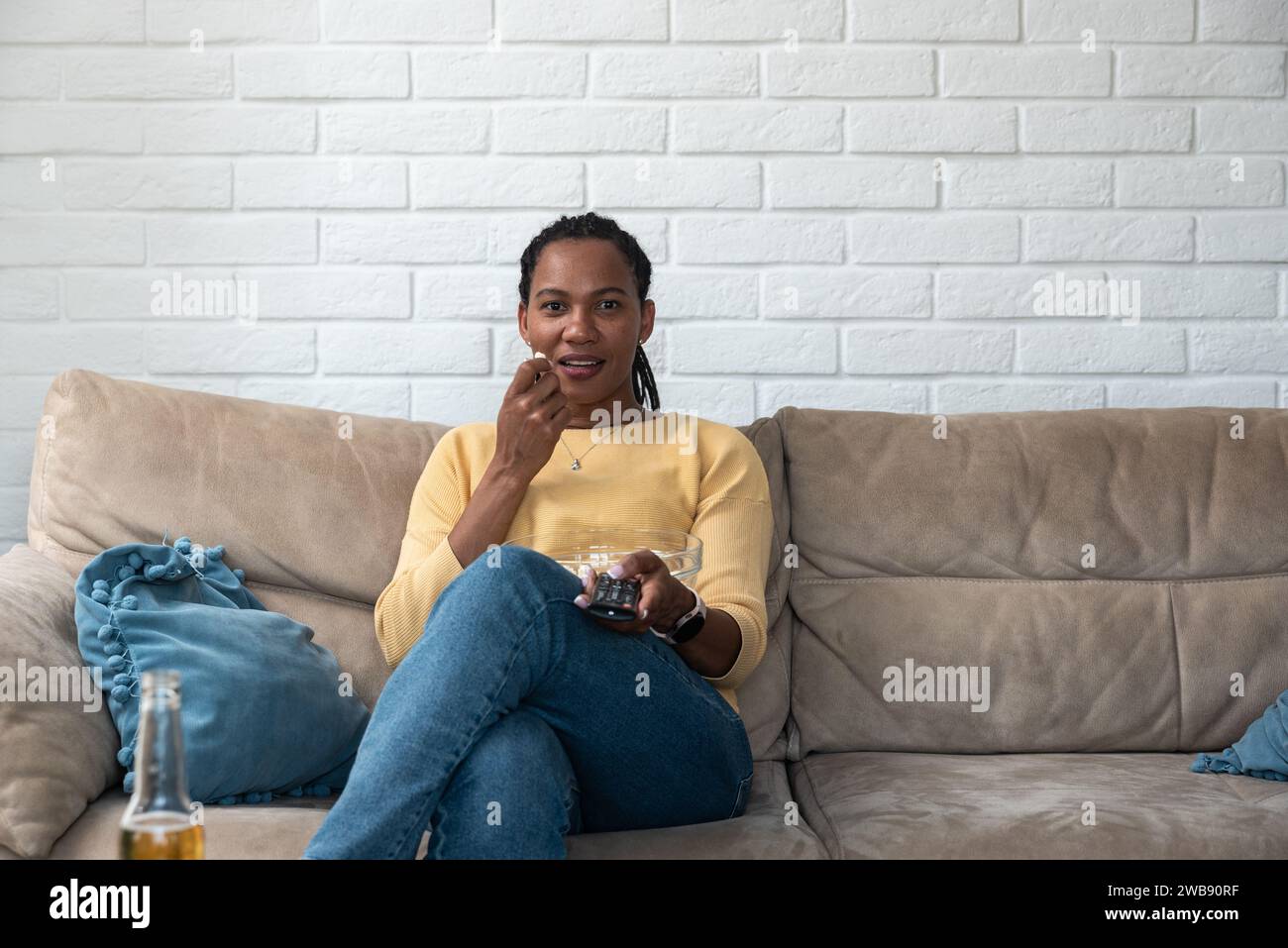 Laughing young pretty African American woman sitting on sofa, eating ...