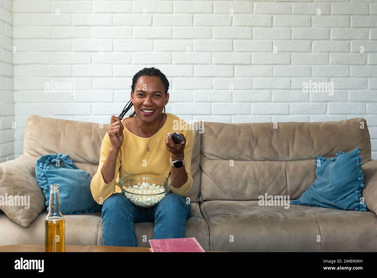 Laughing young pretty African American woman sitting on sofa, eating ...