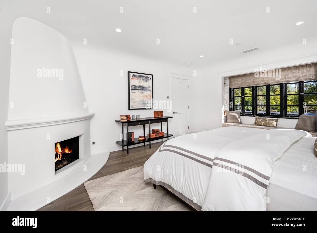 A spacious bedroom features white walls, wood floors, and large windows ...