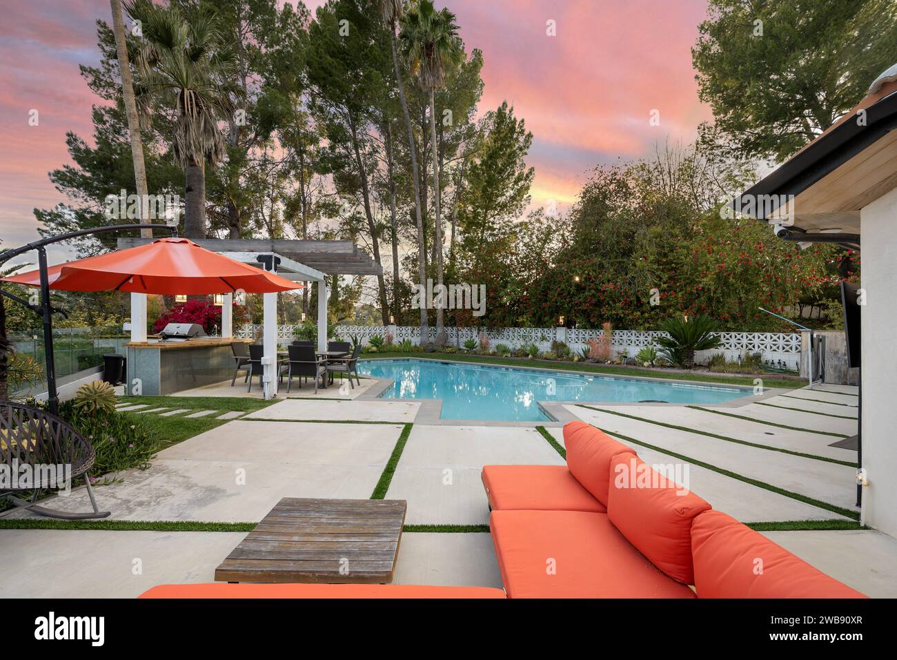 A swimming pool in front of an outdoor patio covered with a roof and ...