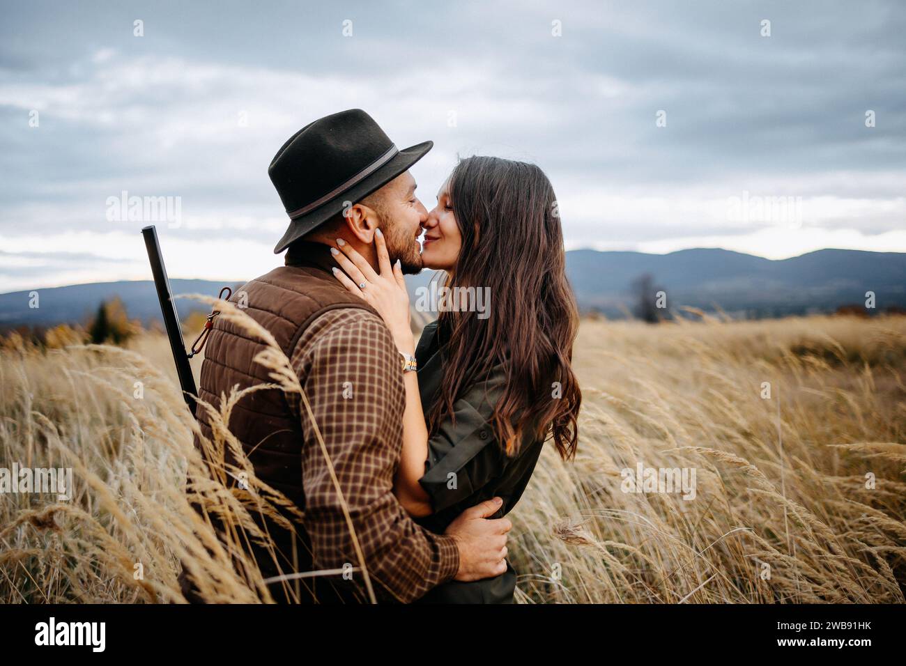 Young lovely couple, the hunter and his lady kissing and embracing each other in a field with ...