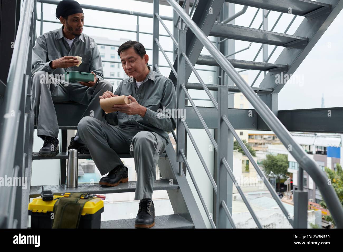 Construction workers in grey uniform sitting on steps and eating lunch ...