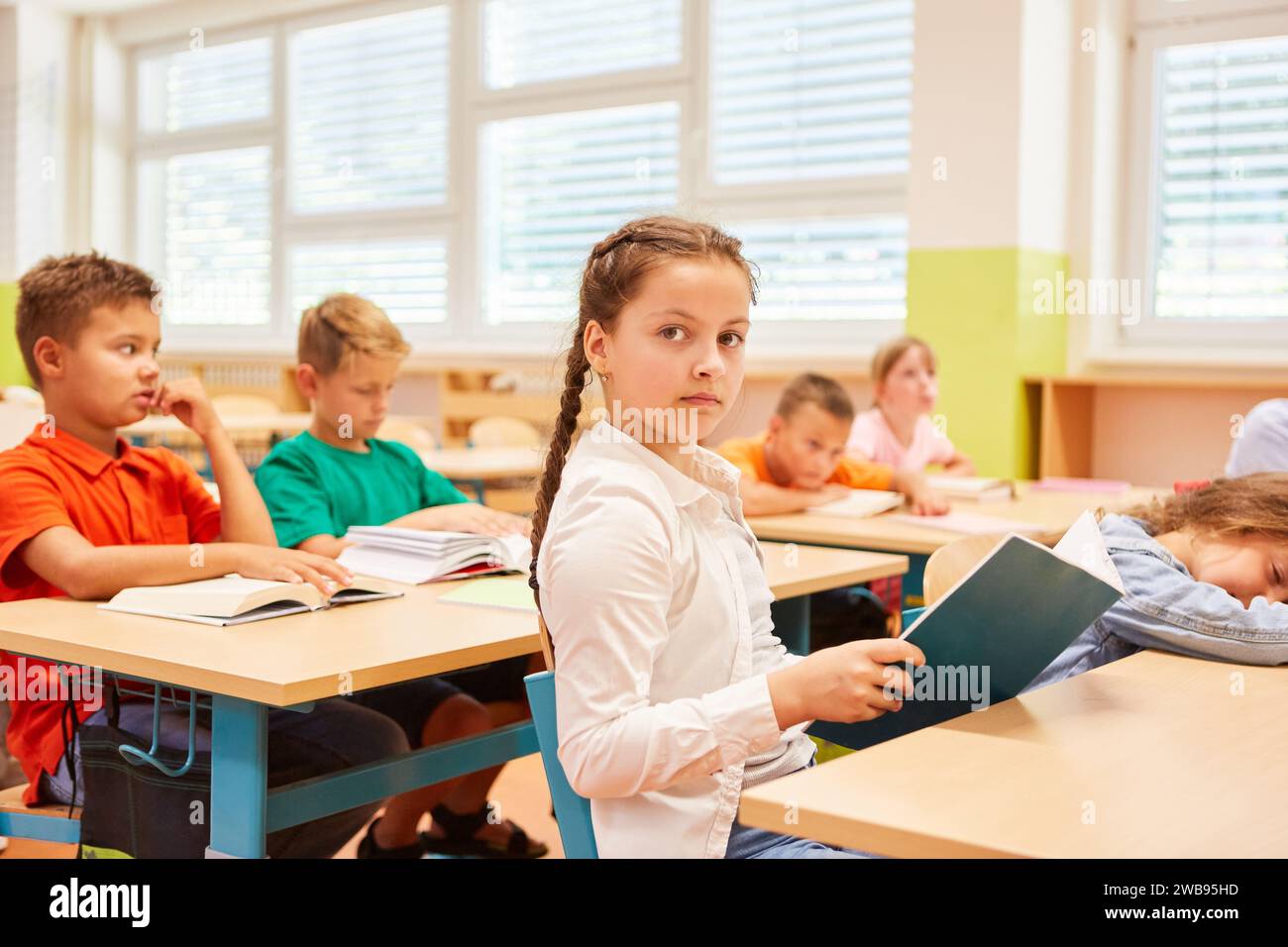 Side view portrait of schoolgirl holding book while sitting on bench ...