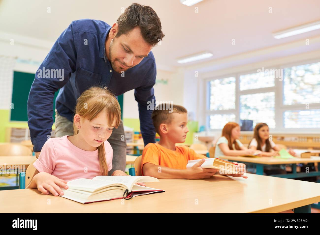 Male teacher assisting female student reading book while sitting at ...