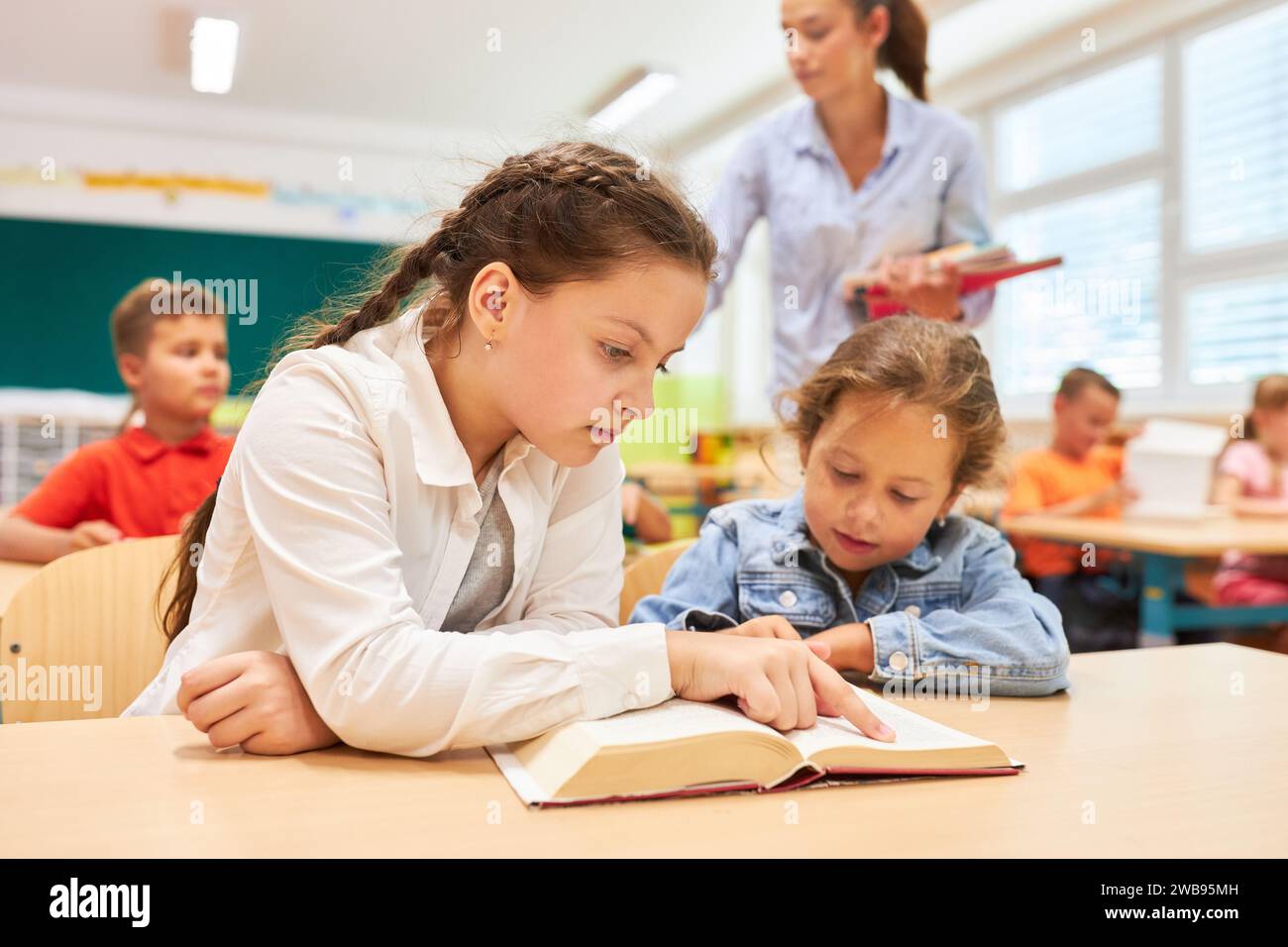 Curious schoolgirls reading book at desk in classroom Stock Photo - Alamy