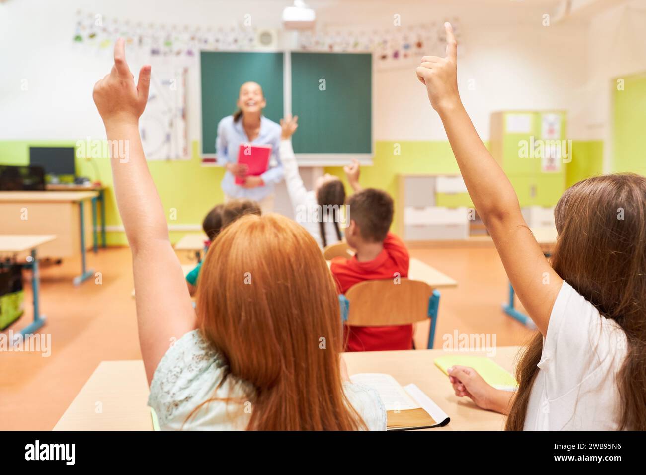 Rear view of girls raising hand while sitting on bench during lecture ...