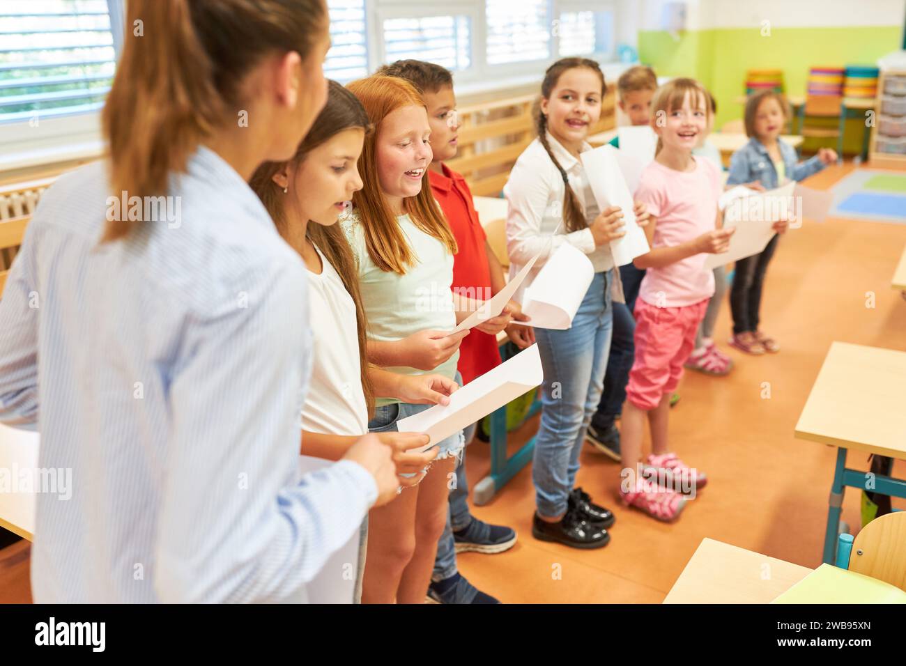 Female teacher standing near students doing choir rehearsal in ...
