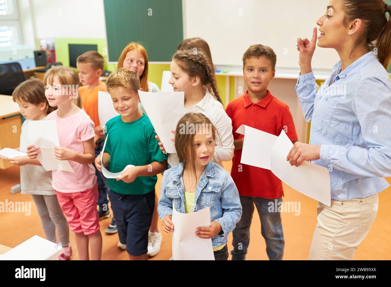 Side view of female teacher rehearsing choir with students in classroom ...