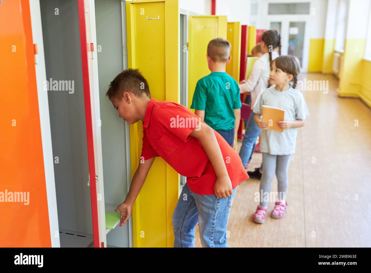 Side view of boy keeping book in locker while standing with classmates ...