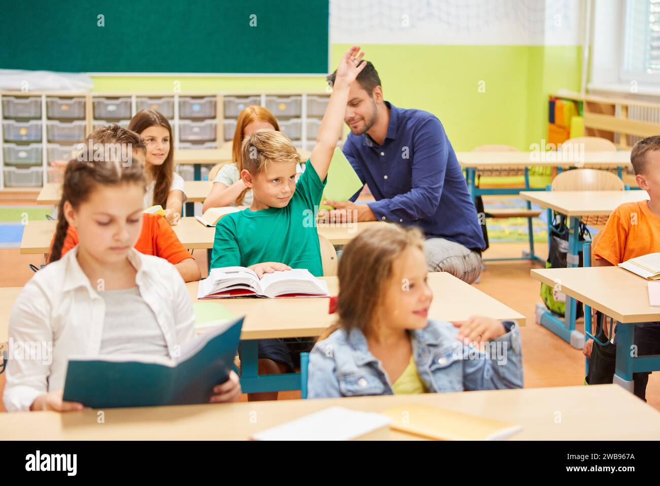Boy raising hand while sitting on bench during lecture in classroom ...