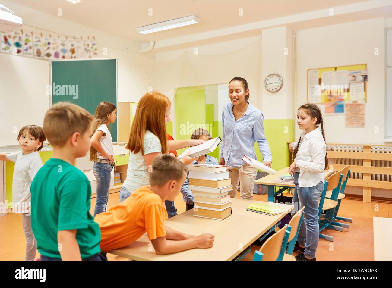 Group of students stacking books on bench with female teacher in class ...