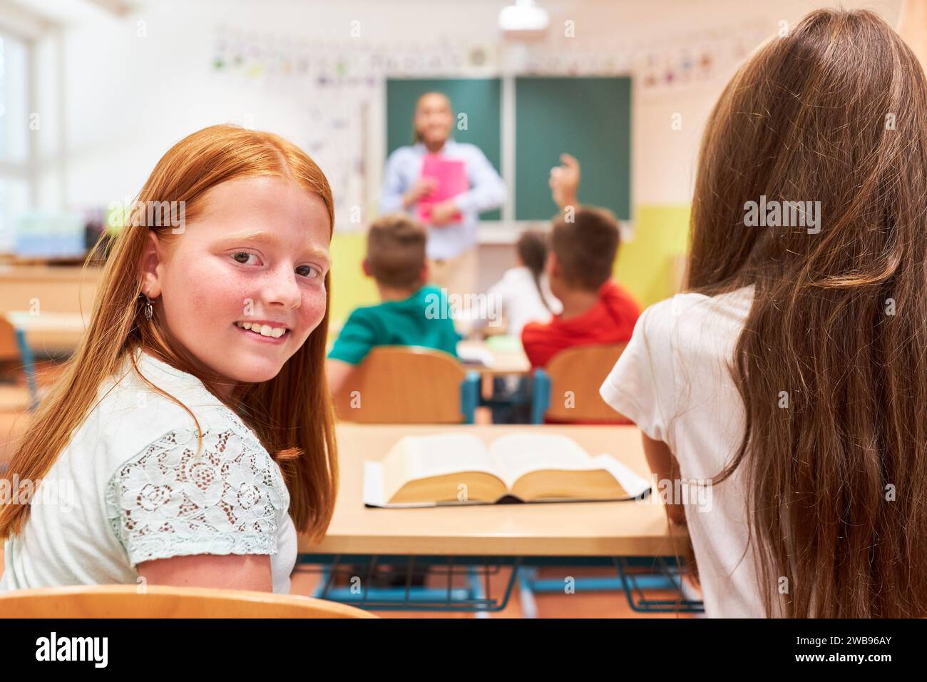Side view portrait of smiling schoolgirl sitting with classmate in ...