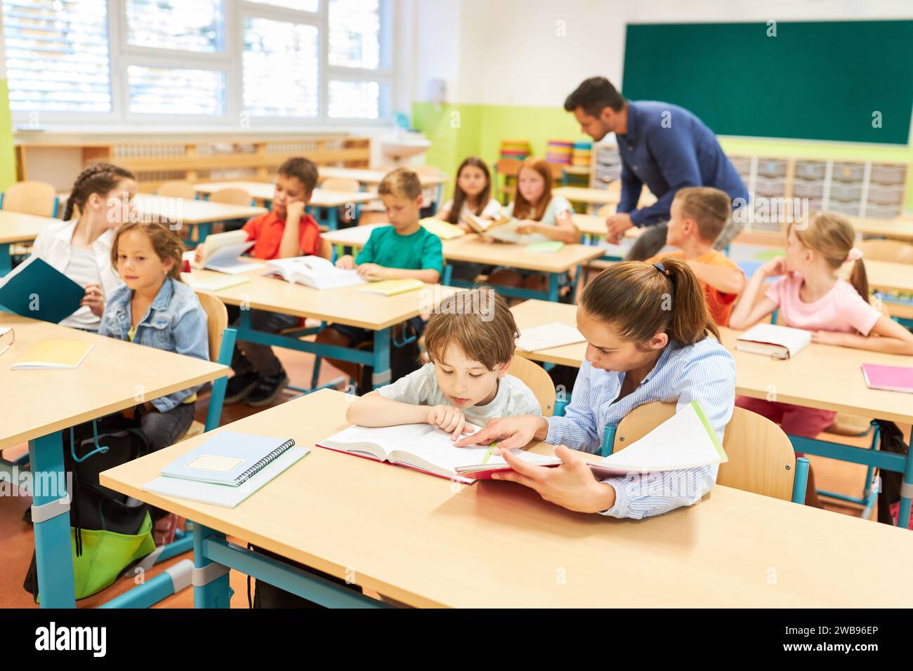 Female teacher reading book to elementary schoolgirl while sitting at ...