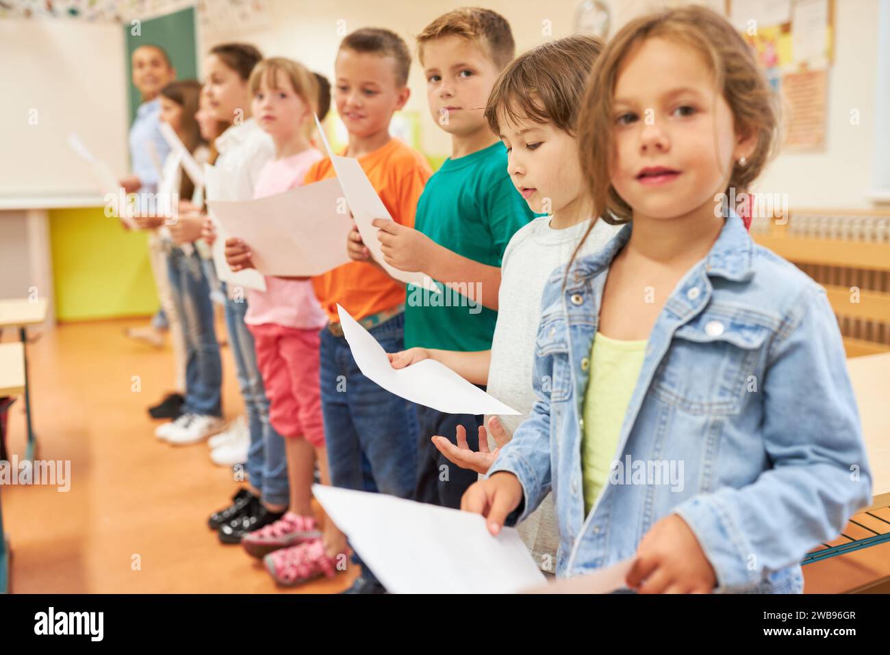 Diverse schoolkids holding sheet during choir rehearsal in classroom ...