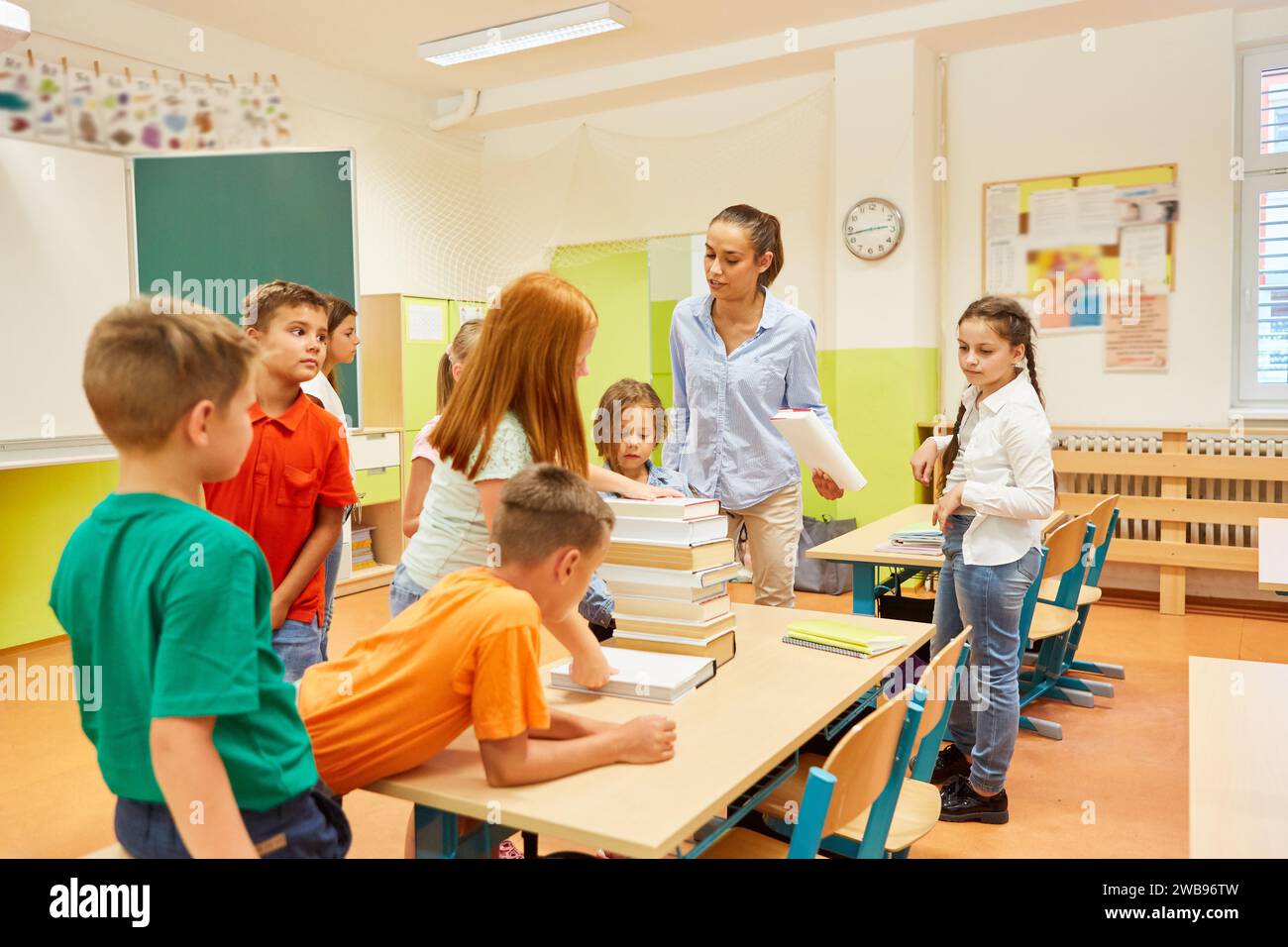 Female teacher stacking books on bench with group of students in ...