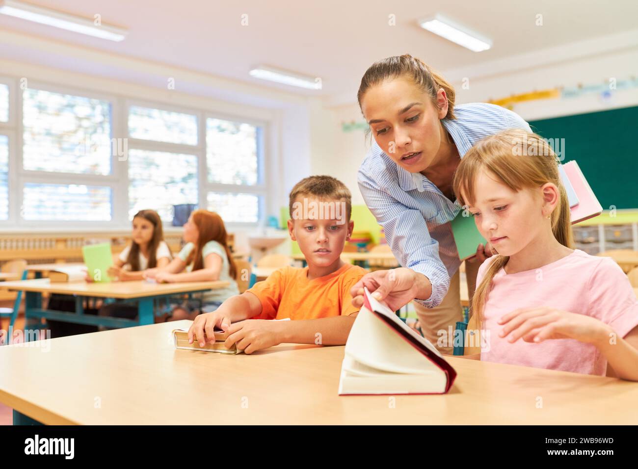 Female teacher reading book to students sitting on bench in classroom ...