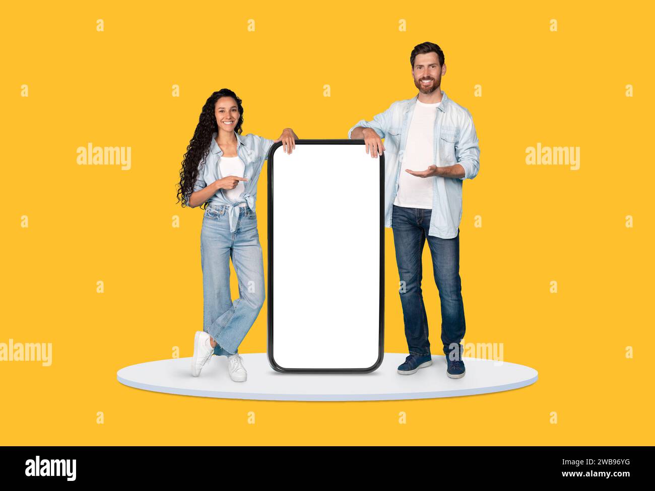 Man and woman presenting large smartphone display on yellow background ...