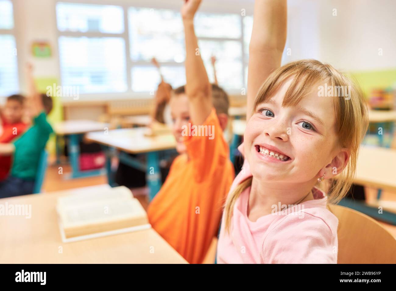 Portrait of blond schoolgirl raising hand during lecture in classroom ...