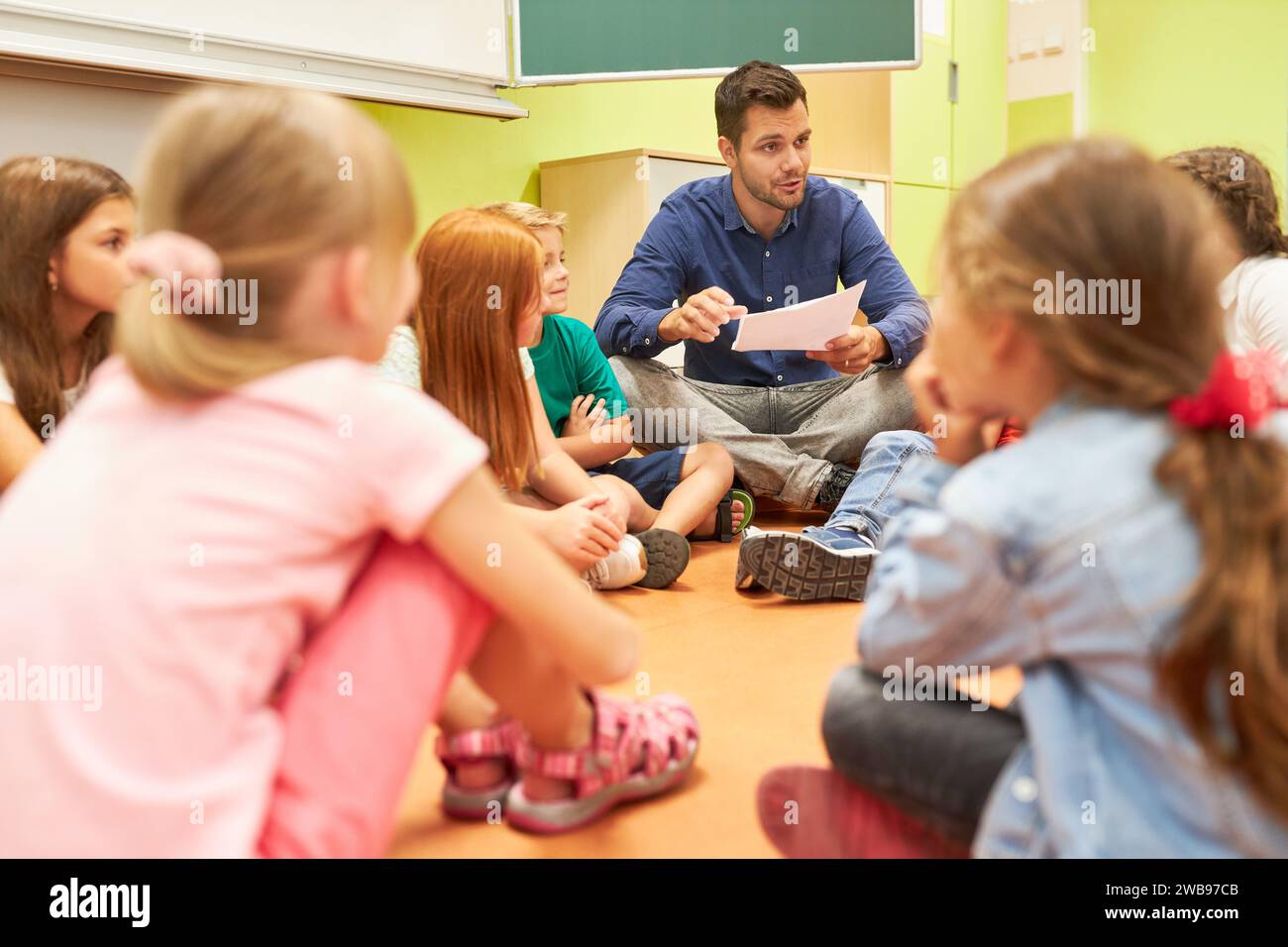 Teacher discussing with group of students sitting on floor in classroom ...